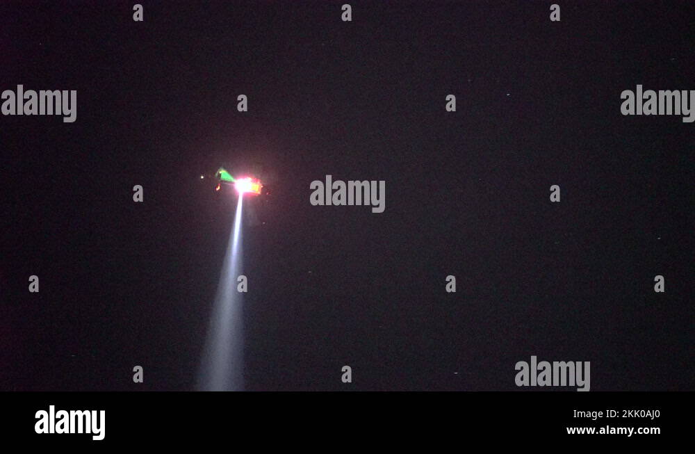 Police helicopter searches from the city night sky with a spotlight ...