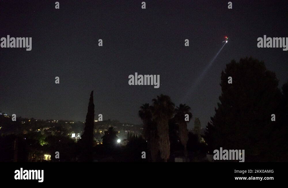 Police helicopter searches from the city night sky with a spotlight ...
