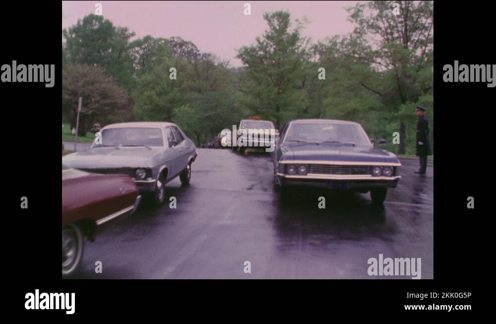 1960s: Cars drive in funeral procession through cemetery. Officers in ...