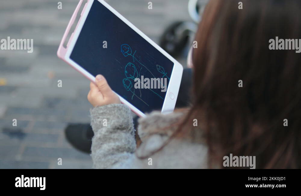 Happy little girl showing her drawings of stick figures on a tablet ...