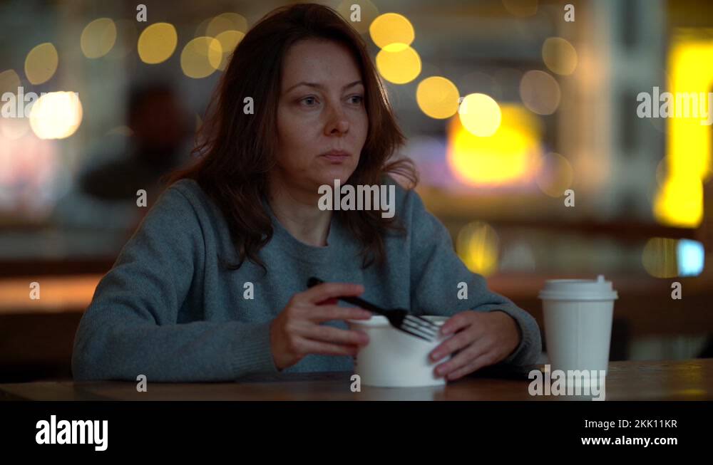 middle-aged woman is dining alone in fast food restaurant, chewing and ...