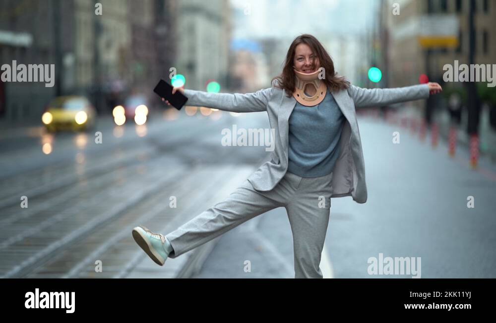 happy and funny woman with neck brace is dancing on city street, curing ...