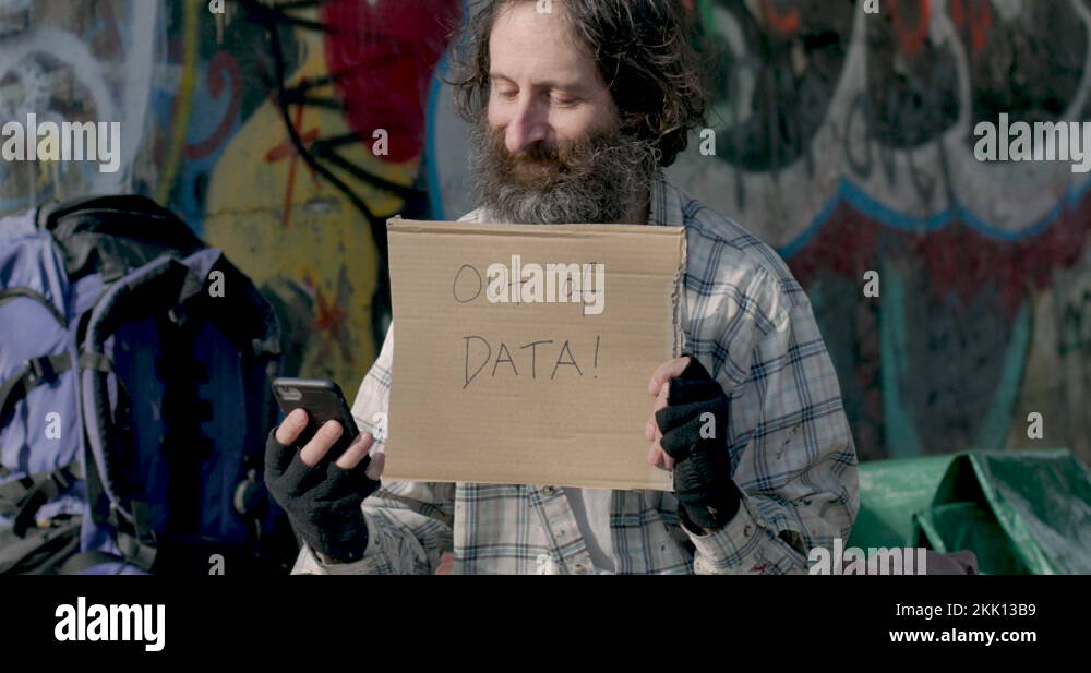 Homeless man holding a sign that says out of data while looking at his ...