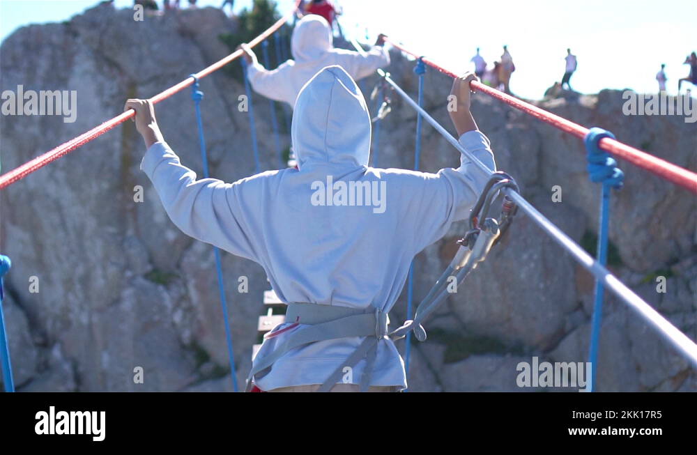 Girls crossing the chasm on the rope bridge. Black sea background ...