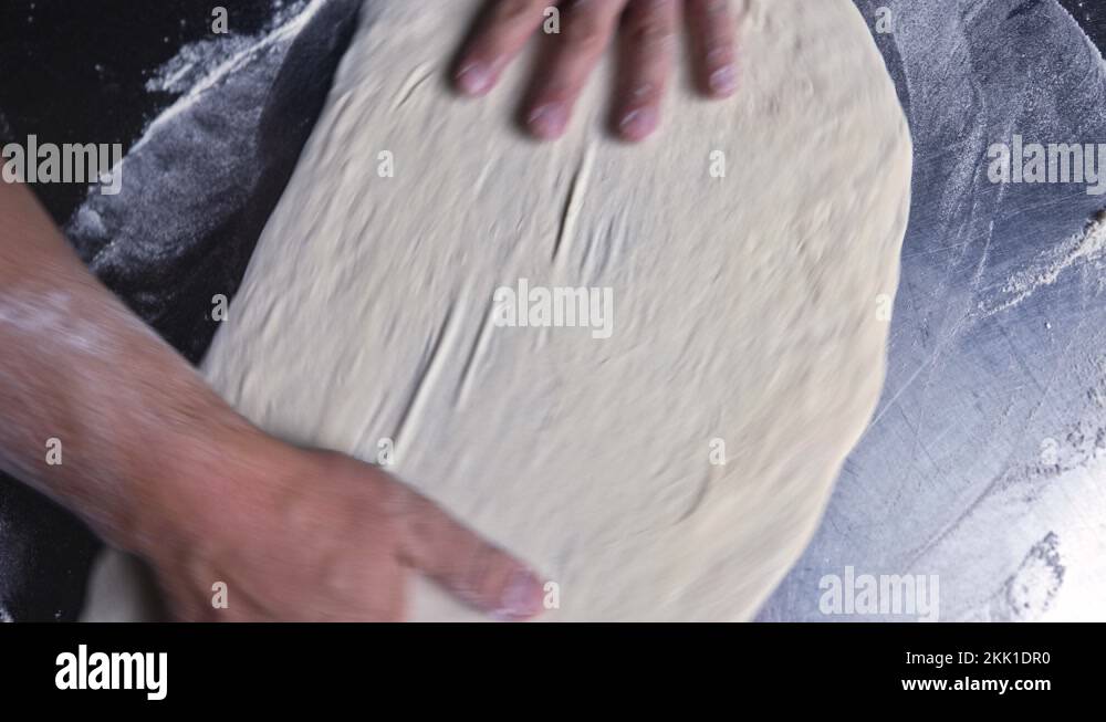 Man chef hands stretching pizza dough to a circle top view zooming out ...