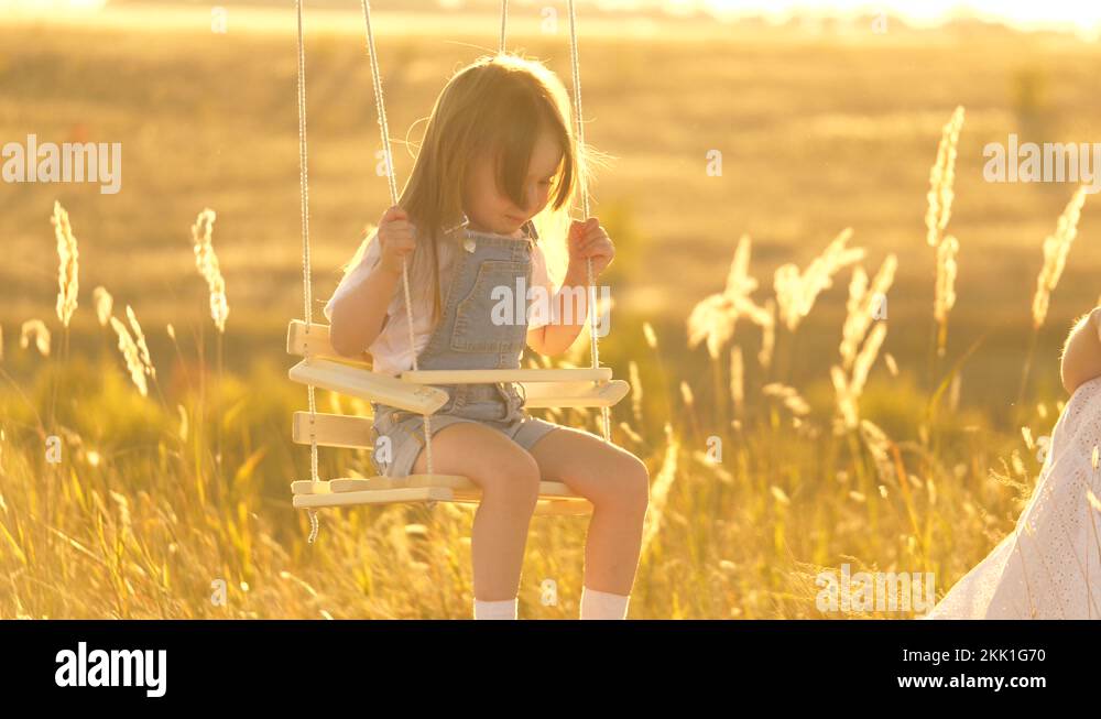 Mom shakes her healthy daughter on a swing under a tree in the sun ...