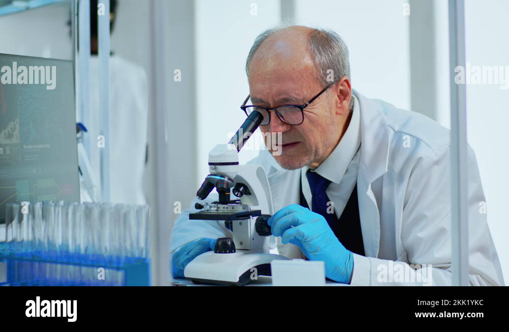 Laboratory scientist conducting experiment looking at microscope in ...