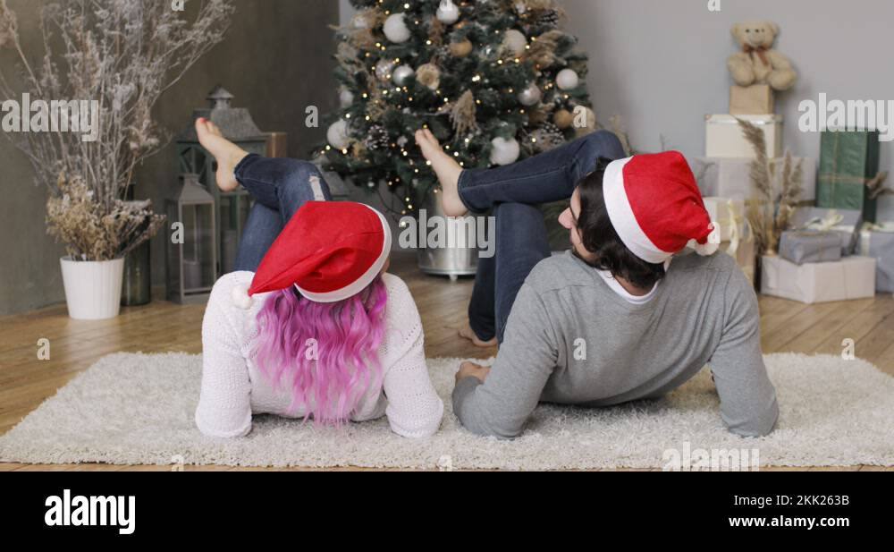 Young Couple In Santas Red Hats Lying Together Near Christmas Tree