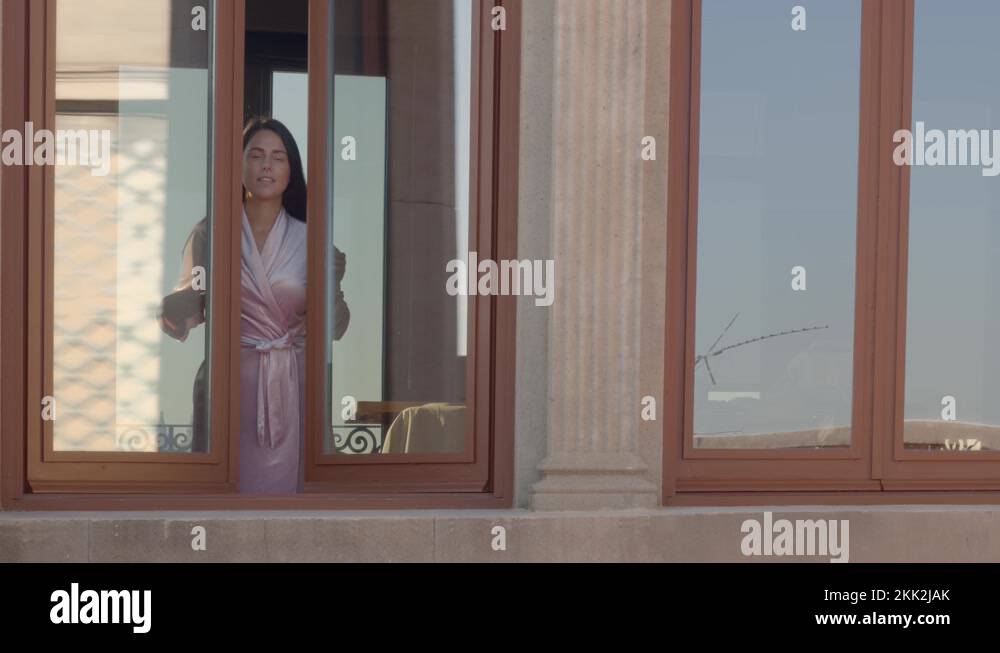 Beautiful woman in a pink robe, opening big windows. Still medium-long ...