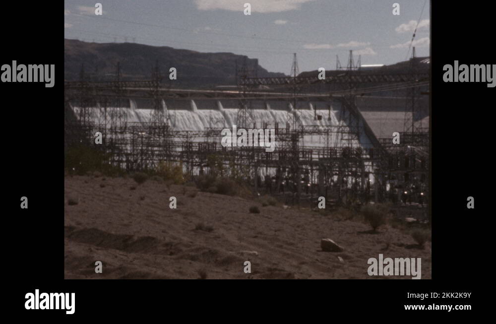 1950s: water flows heavily over dam with electrical power plant in ...