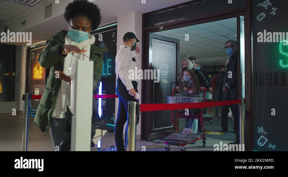 Diverse crowd walking past guard with thermometer and disinfecting ...