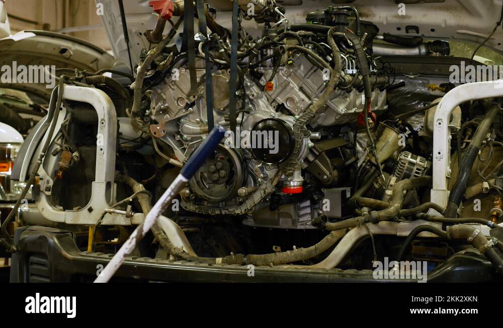 A mechanic pushes a engine into an empty engine bay cavity on a truck ...