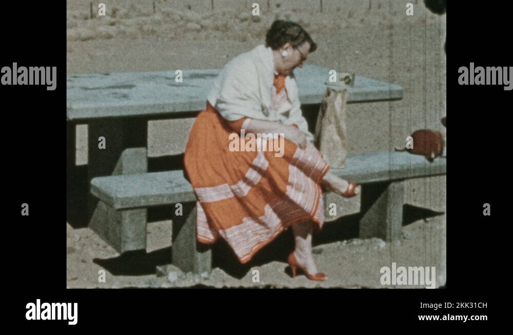 1950s: Plump woman empties shoe, drinks from thermos at roadside table ...