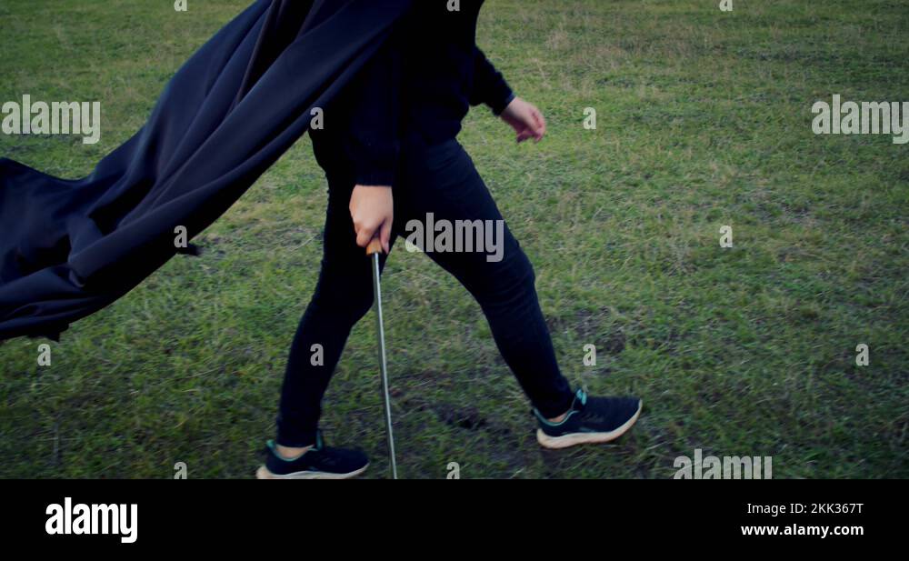 Creepy evil witch in black clothes and a cape is walking with a sword ...
