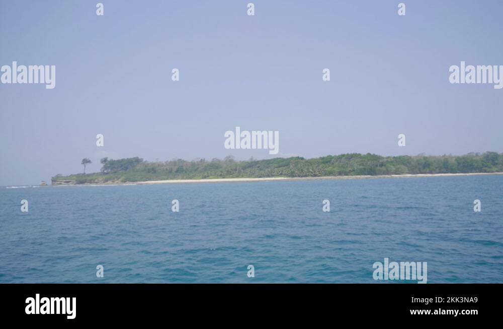 Sailing past the peninsula of a remote island with azure blue sea white ...