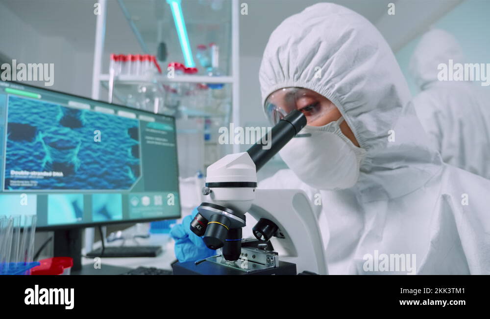 Nurse in ppe suit doing medical experiments using microscope Stock ...