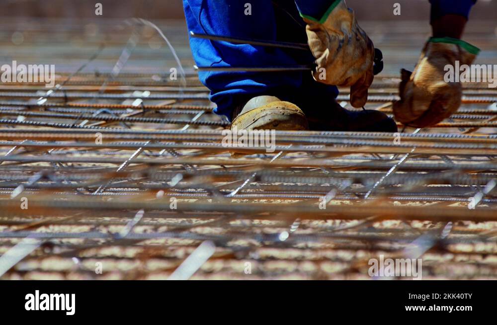 Tying rebar with wire in a grid before pouring a concrete foundation ...