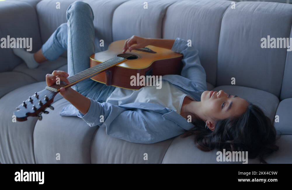 Girl playing guitar on sofa. Relaxed musician playing chords on ...