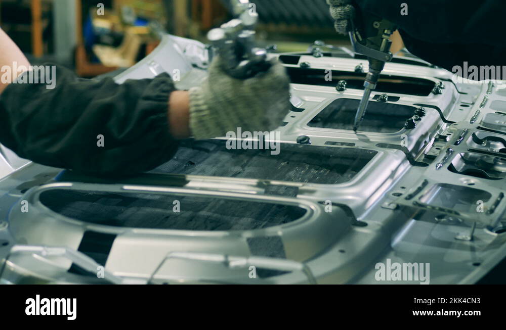 Couple of car factory workers applying structural adhesive on car body ...