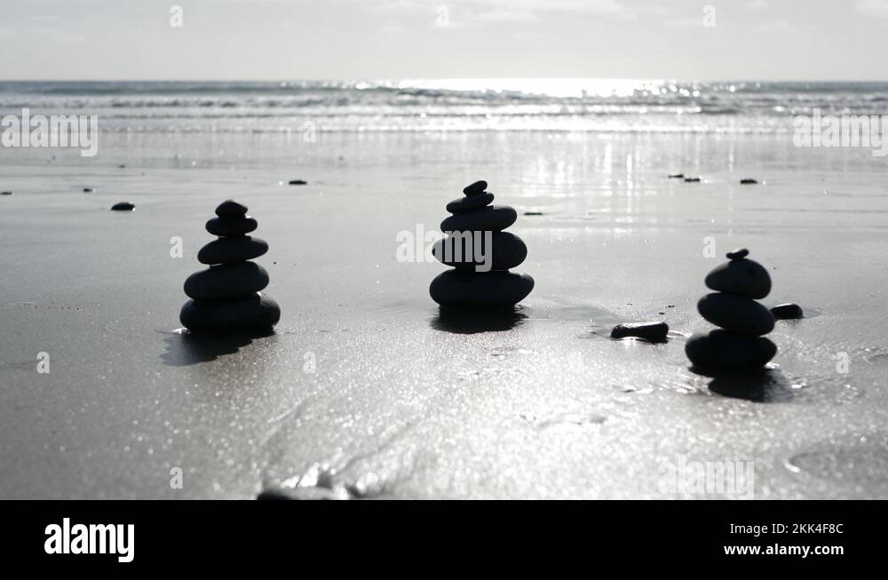Rock balancing on ocean beach, stones stacking by sea water waves ...