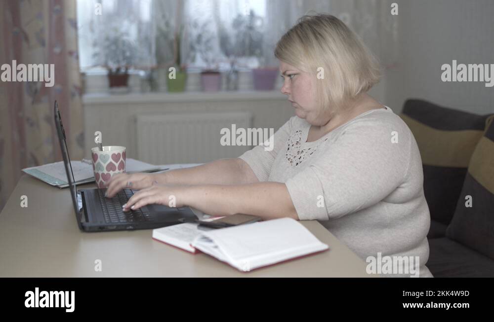 Overworked fat woman works at her desk in the home office. She types ...