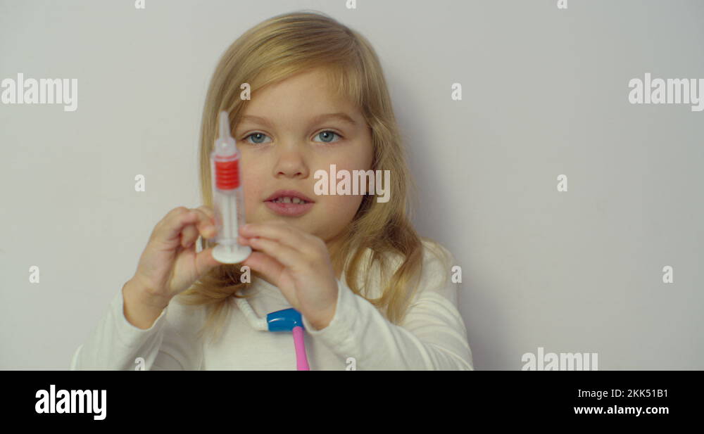 Little child girl wear red glasses holding toy medical syringe playing ...