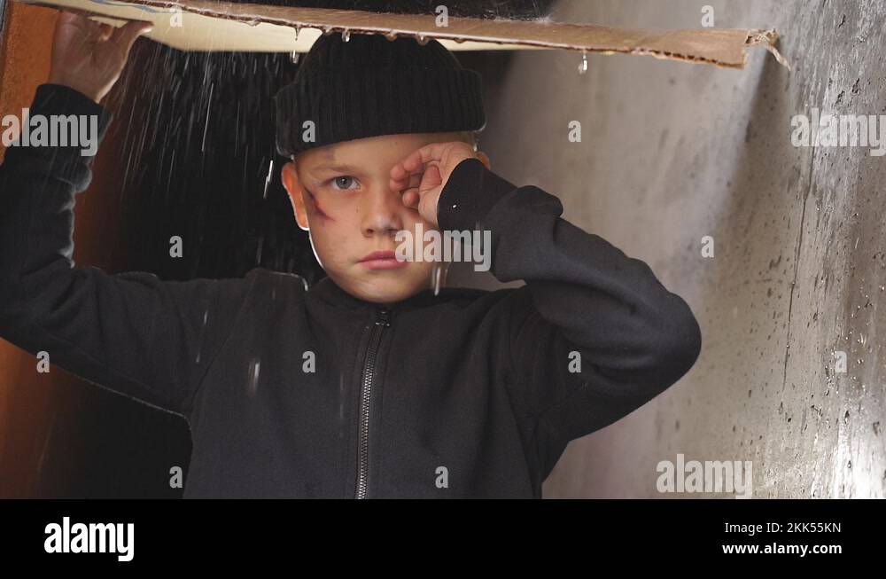 Poor orphan boy shelters from the rain under cardboard, crying Stock ...