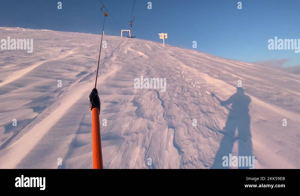 Snowboarder being pulled uphill by a t-bar drag lift at a ski resort ...