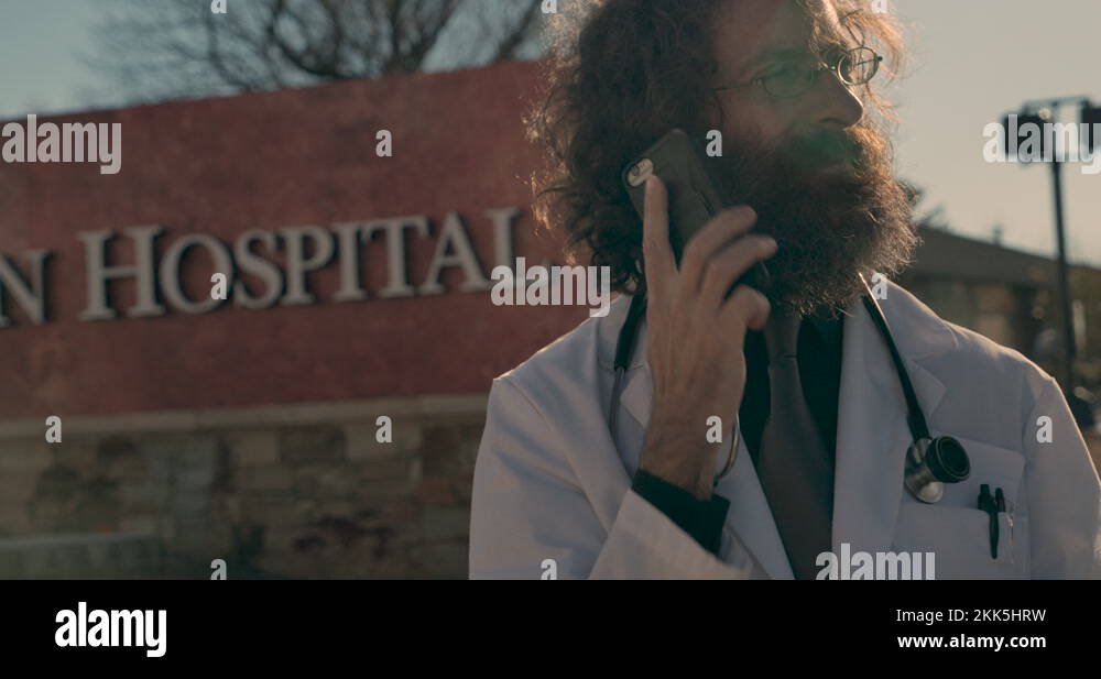 Male doctor standing outside in front of a Hospital sign using his ...
