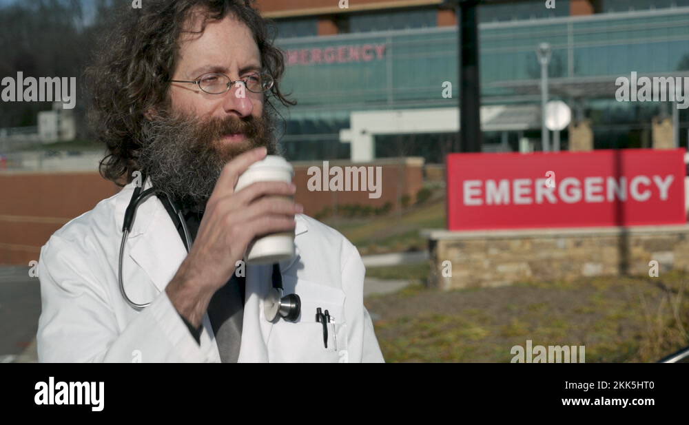 Tired, exhausted male doctor drinking coffee outside of an emergency ...