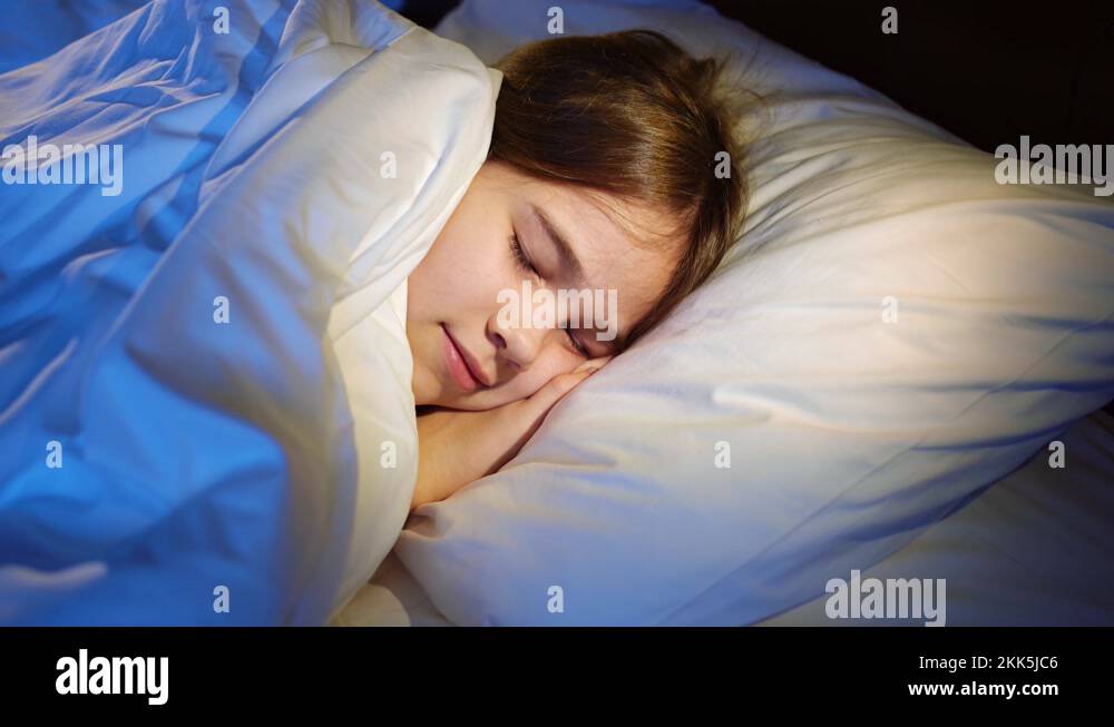 The pretty teenage girl naps in bed, sees a pleasant sleep and smiles ...