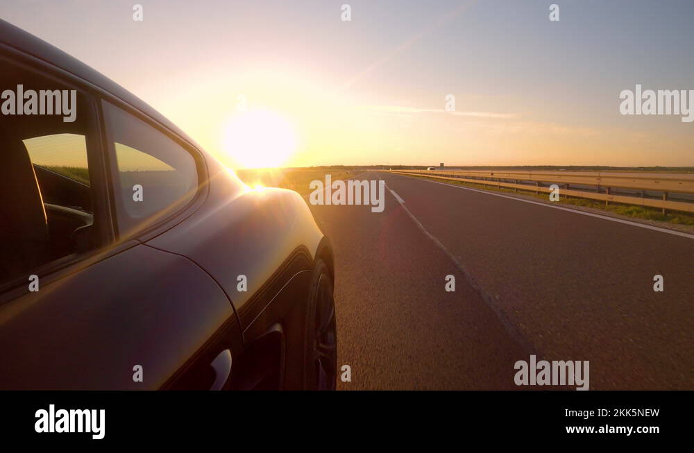 CLOSE UP: Sunrise illuminates the black sportscar cruising along a ...