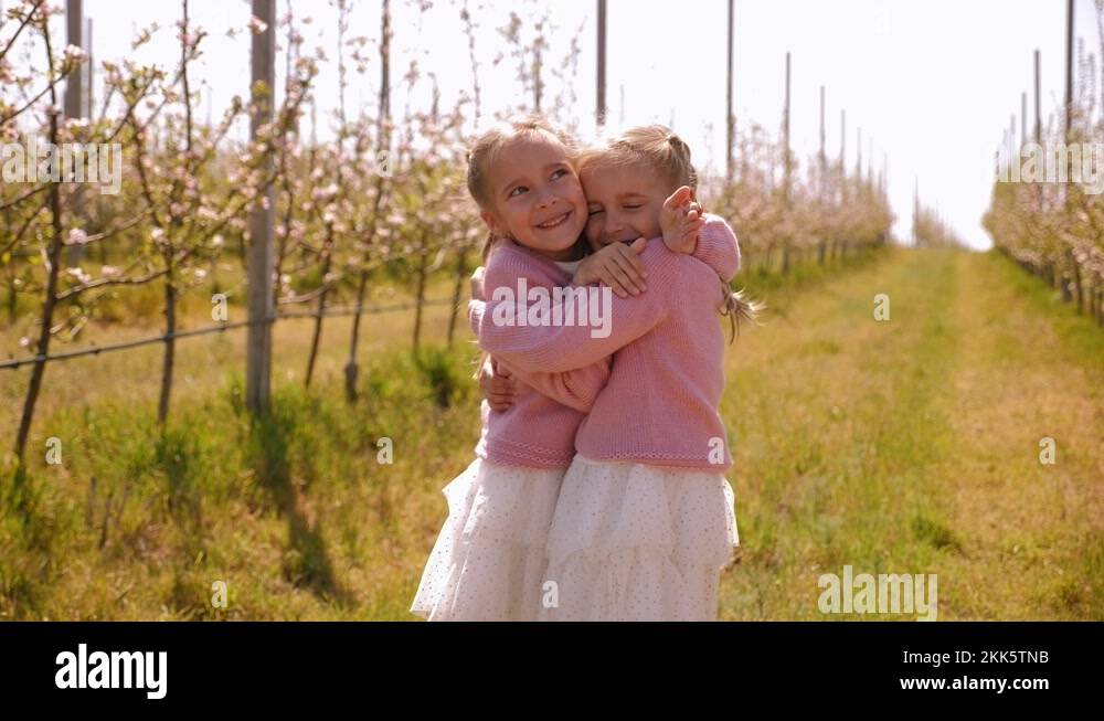 Two little twin sisters dressed in identical dresses hug in an Apple ...
