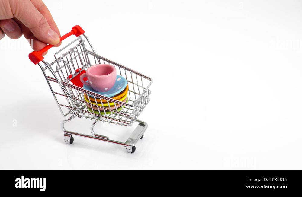 Hand pushing miniature toy supermarket trolley. In the cart is a set of ...