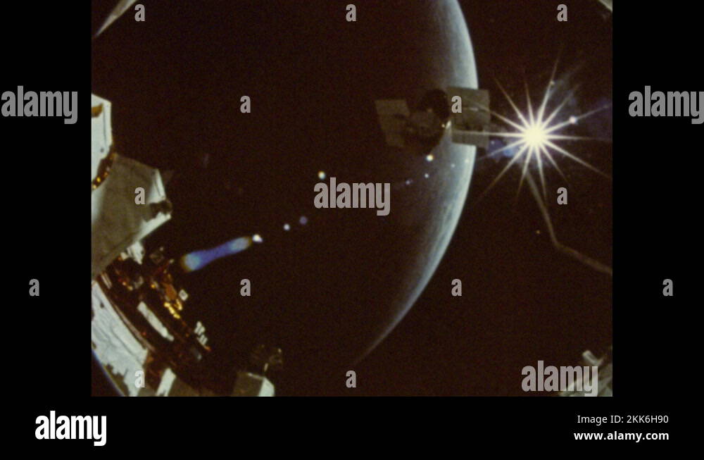1980s: Space shuttle in orbit above earth. Man assembles cylindrical ...
