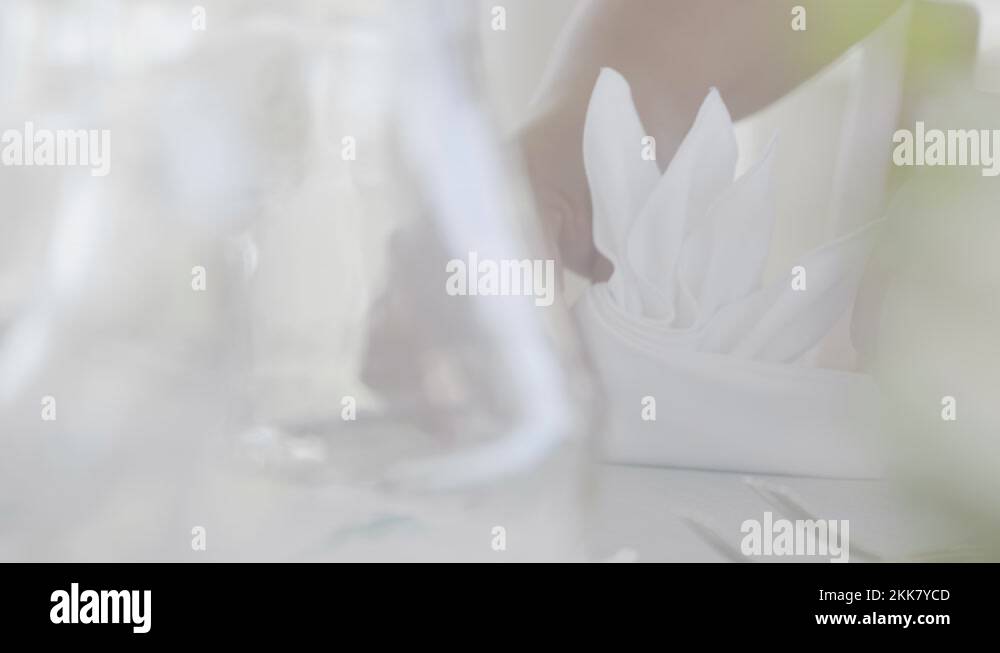 A waiter is arranging and setting a white napkin on a fancy table at a ...