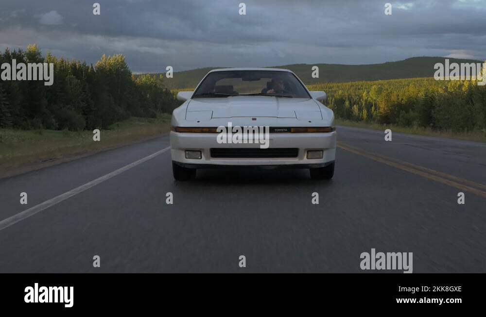 A white Toyota Supra sports car pulls up fast from a far to a camera ...