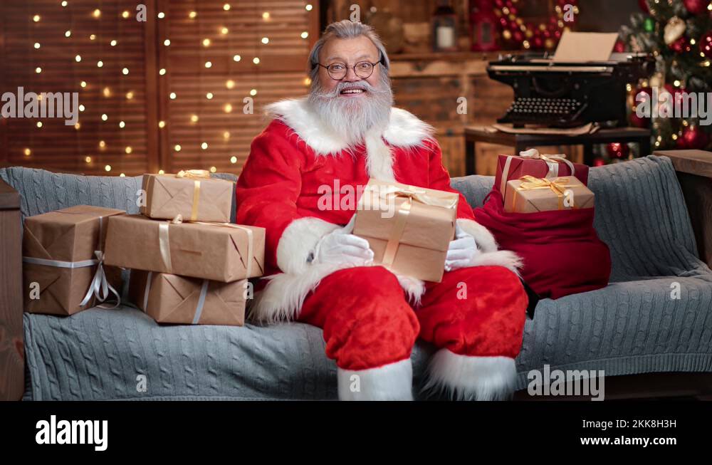 Handsome male Santa Claus posing with gift boxes at illuminated garland ...