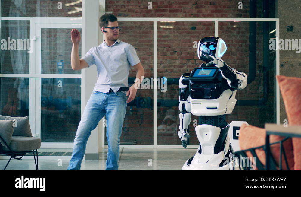 A man is teaching a human-like robot how to dance. Futuristic cyborg ...