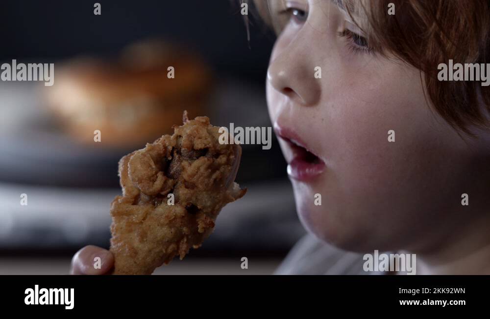 little girl is eating fried chicken leg in fast food restaurant ...