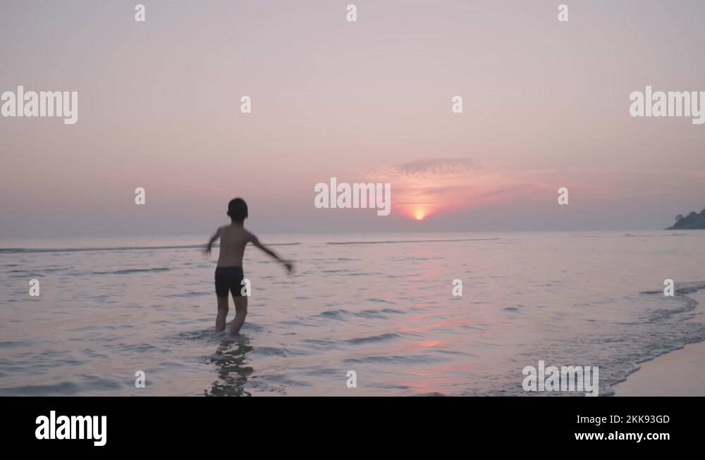An Asian boy in a black swimsuit jumps for joy with the sunrise sky at ...
