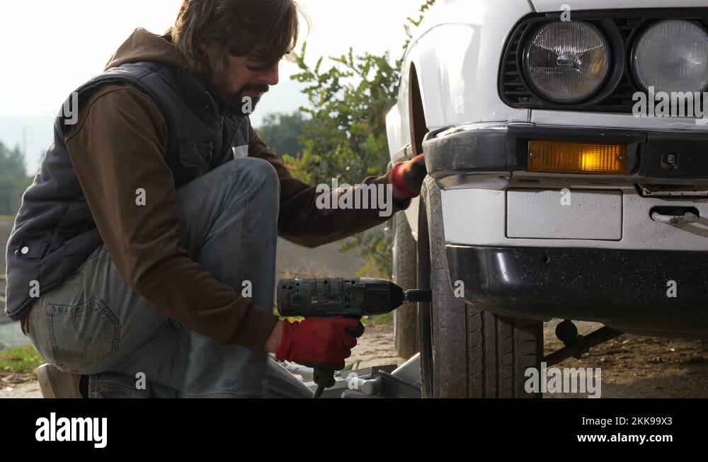 Kneeling man repairing car wheel tightening nuts with hydraulic spanner ...