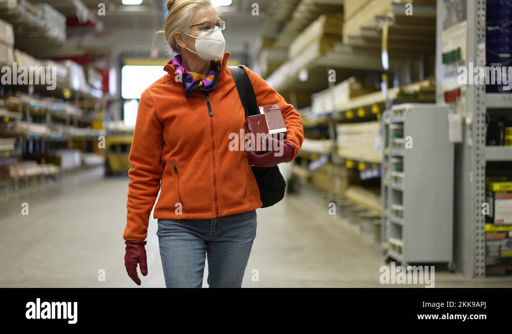 Mature woman wearing face mask walking through the lumber section of a ...