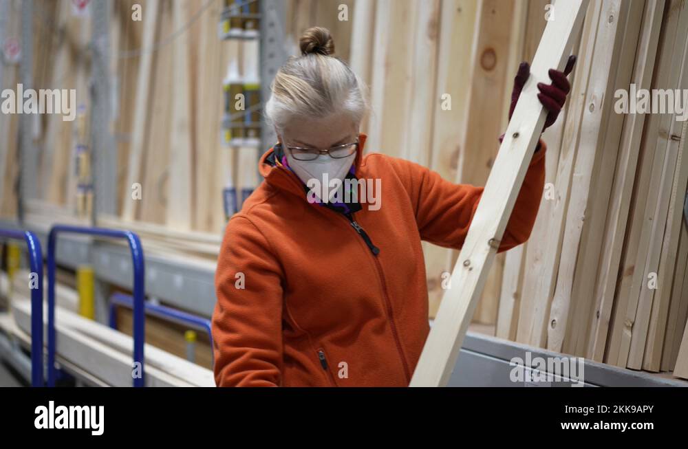 Mature woman wearing face mask looking at wood beams in the lumber ...
