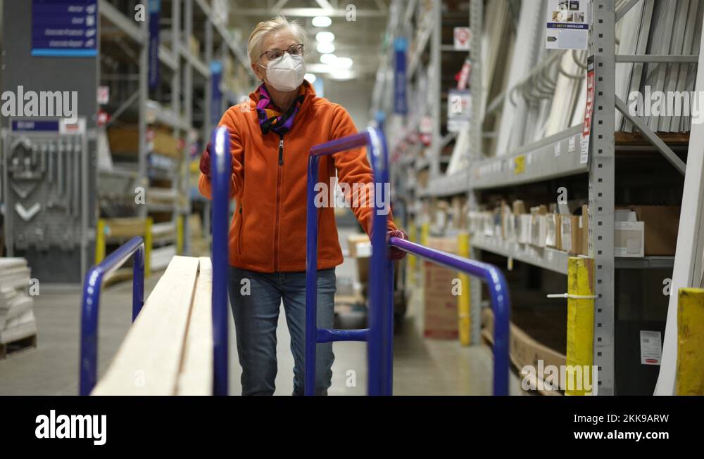 Mature woman wearing face mask pushing a cart in the lumber section of ...
