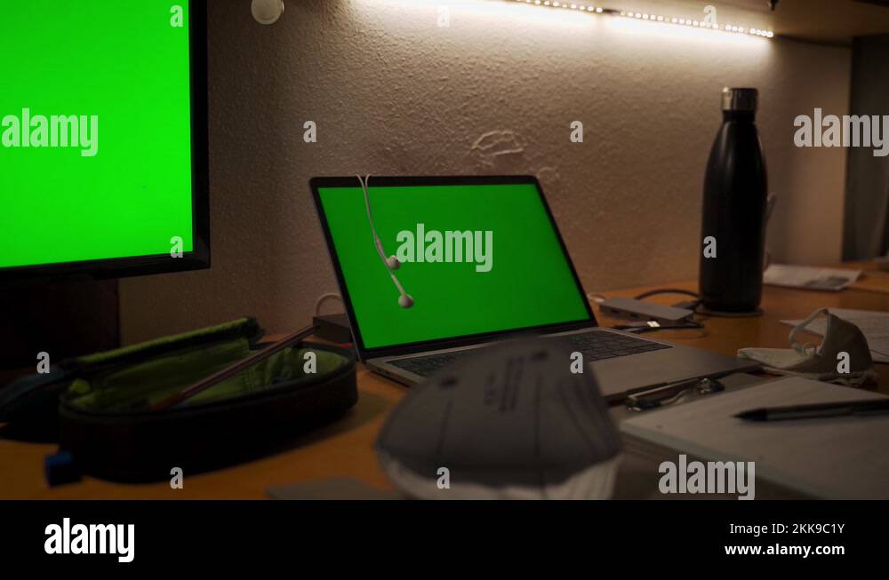 A messy desktop with a green-screen computer and display, a mask, stuff ...