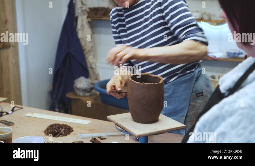 A master potter scrapes the side of her clay pot as she creates a new ...