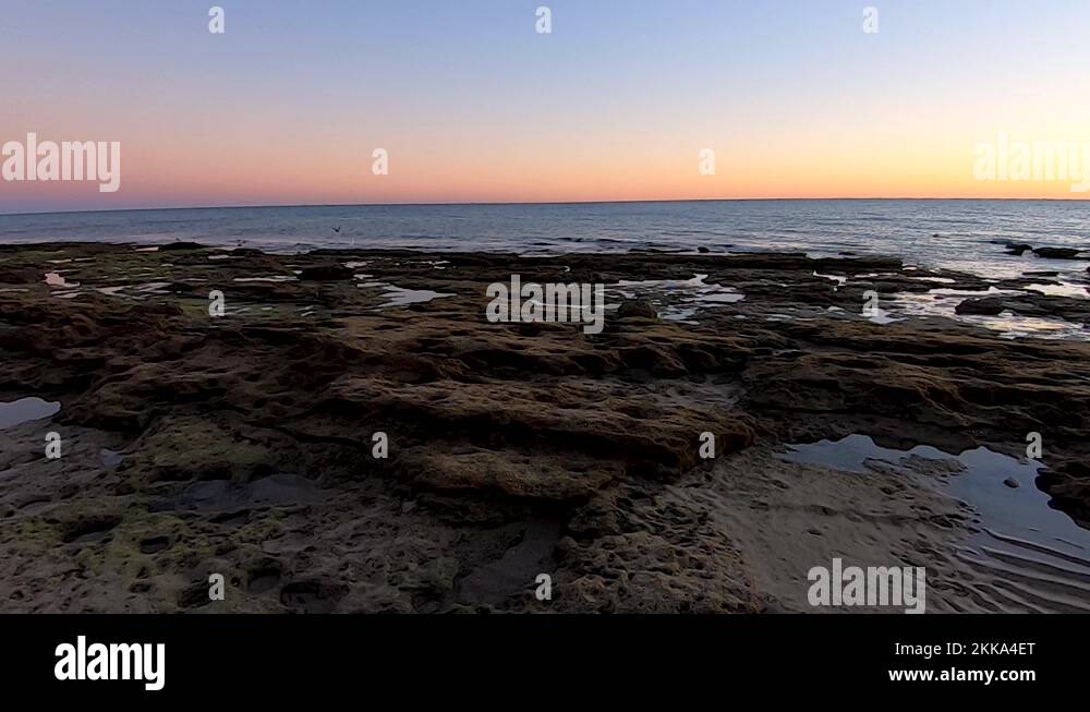 Sea birds fly by in the distance as the sunsets on the tide pools of ...