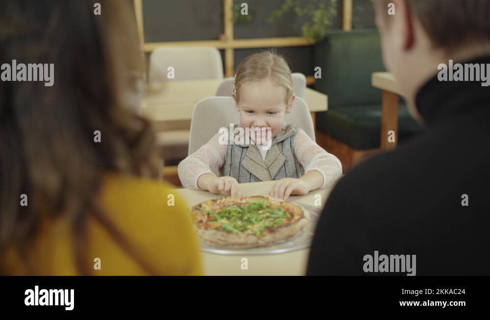 Cheerful charming little girl clapping as waiter bringing pizza in ...