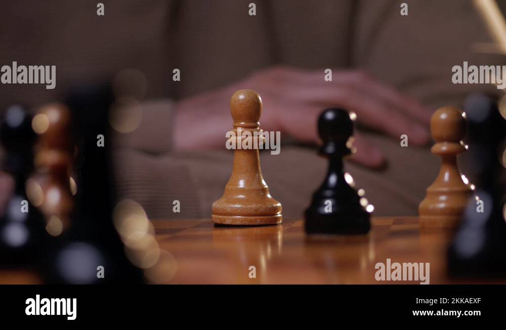 Close-up of wooden classical chess pieces. In the frame, the hand of a ...